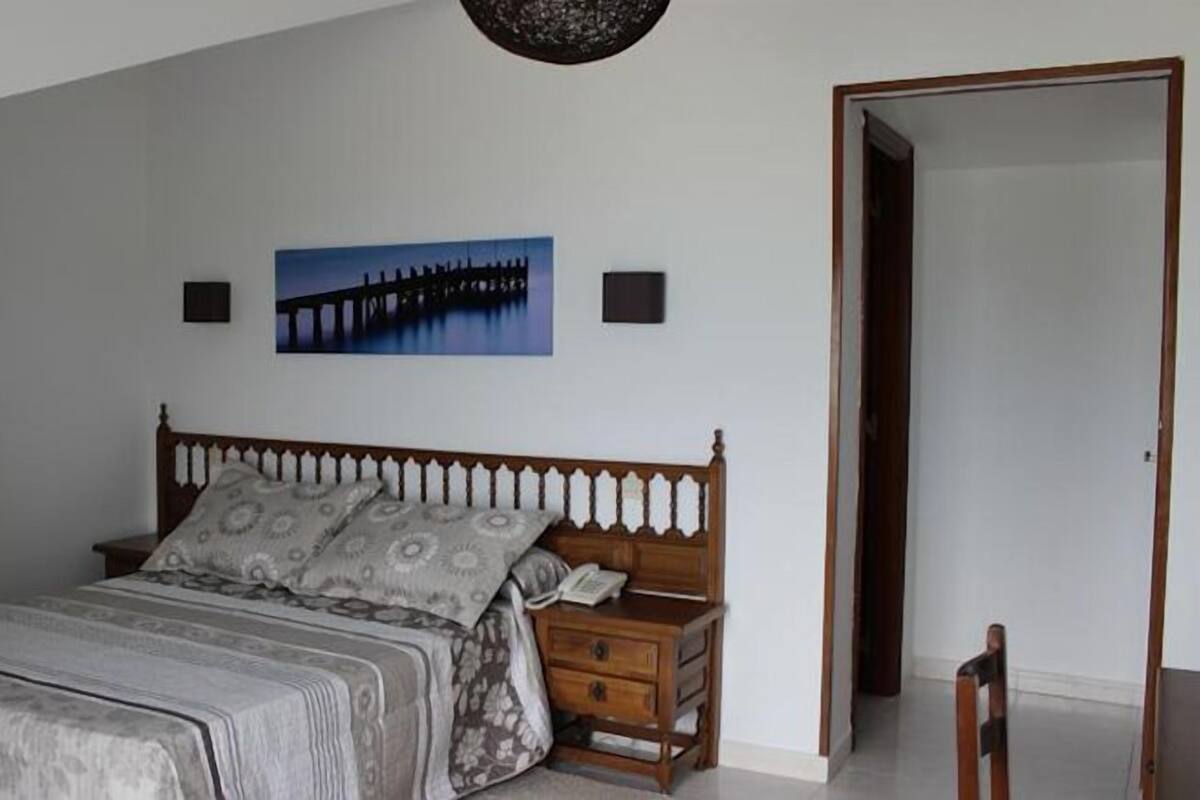 Um quarto com uma cama de madeira, uma mesa de cabeceira, uma cômoda e um quadro de um cais na parede.