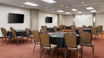 Sala de conferências com mesas redondas, cadeiras, tela de projetor e televisão de tela plana.