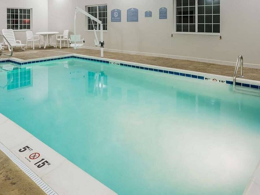Piscina com indicador de profundidade de 1,5 metro, cadeiras de descanso brancas e uma mesa pequena.