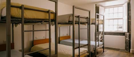Um quarto de dormitório com beliches, uma janela com cortinas e um radiador.