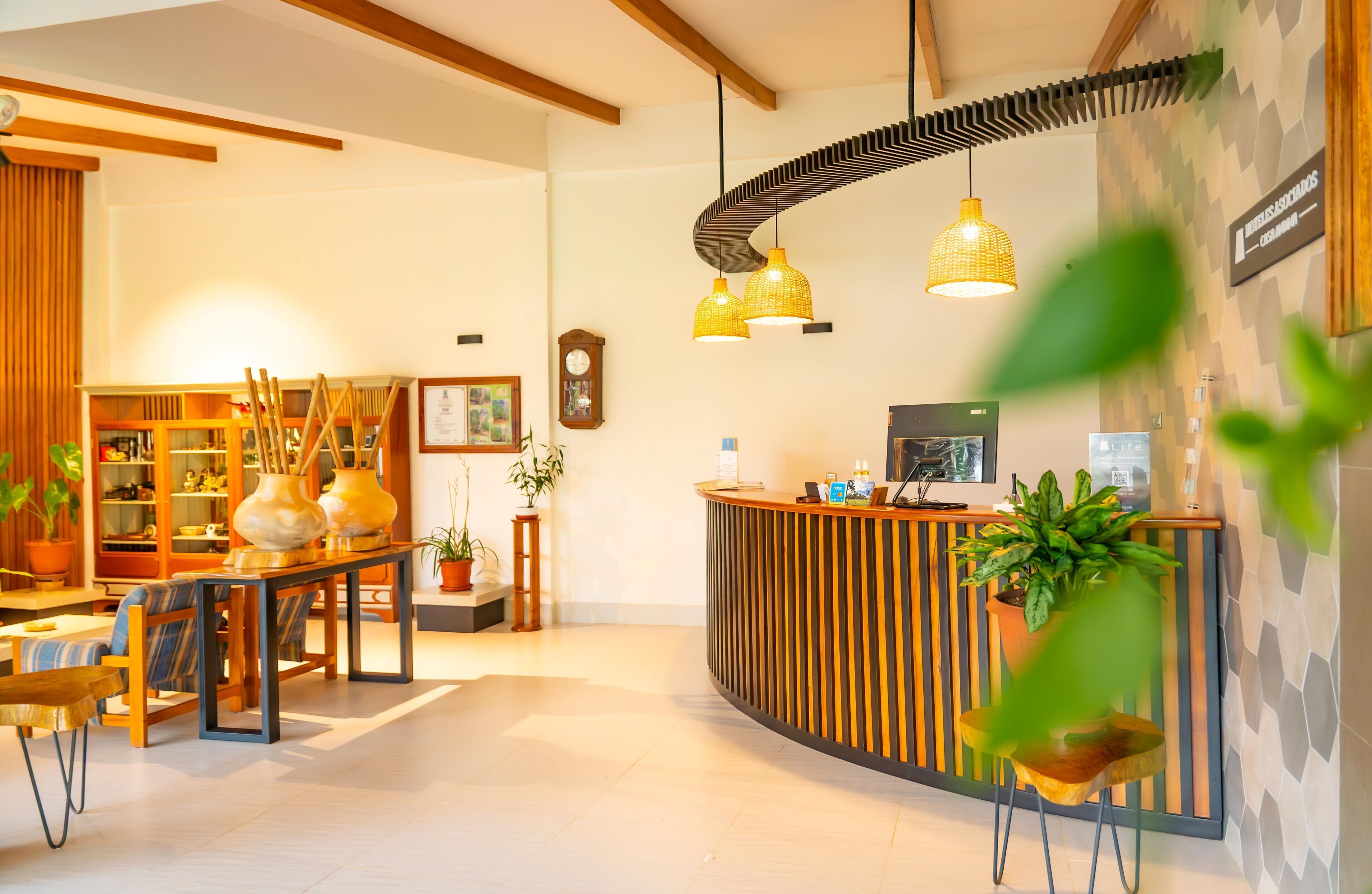 Uma área de recepção com uma mesa de madeira curva, duas luminárias pendentes, um relógio e uma estante.