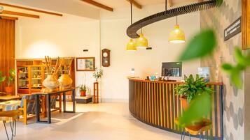 Uma área de recepção com uma mesa de madeira curva, duas luminárias pendentes, um relógio e uma estante.