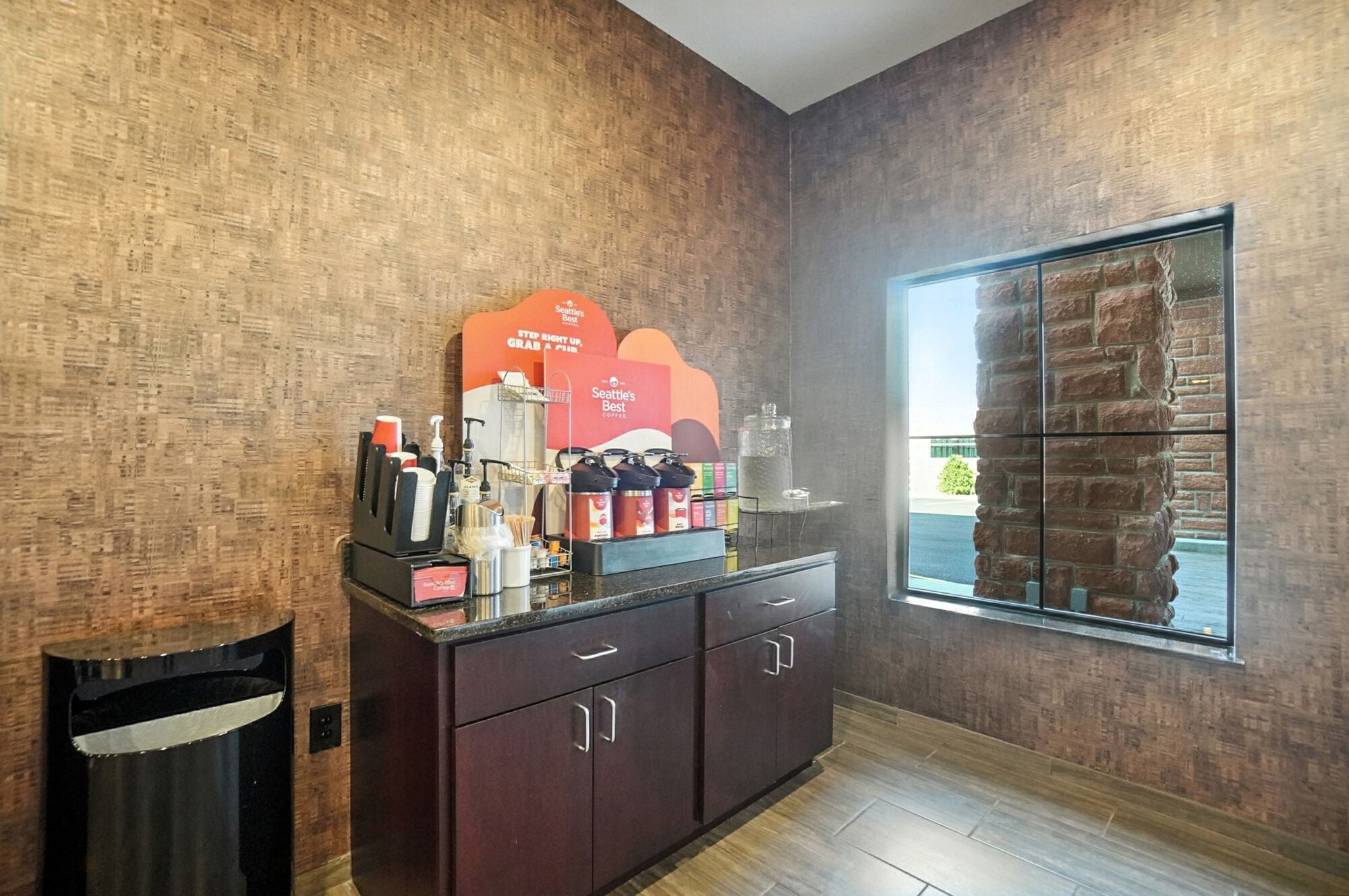 Uma estação de café com recipientes da marca Seattle's Best, uma máquina de café e uma lixeira.