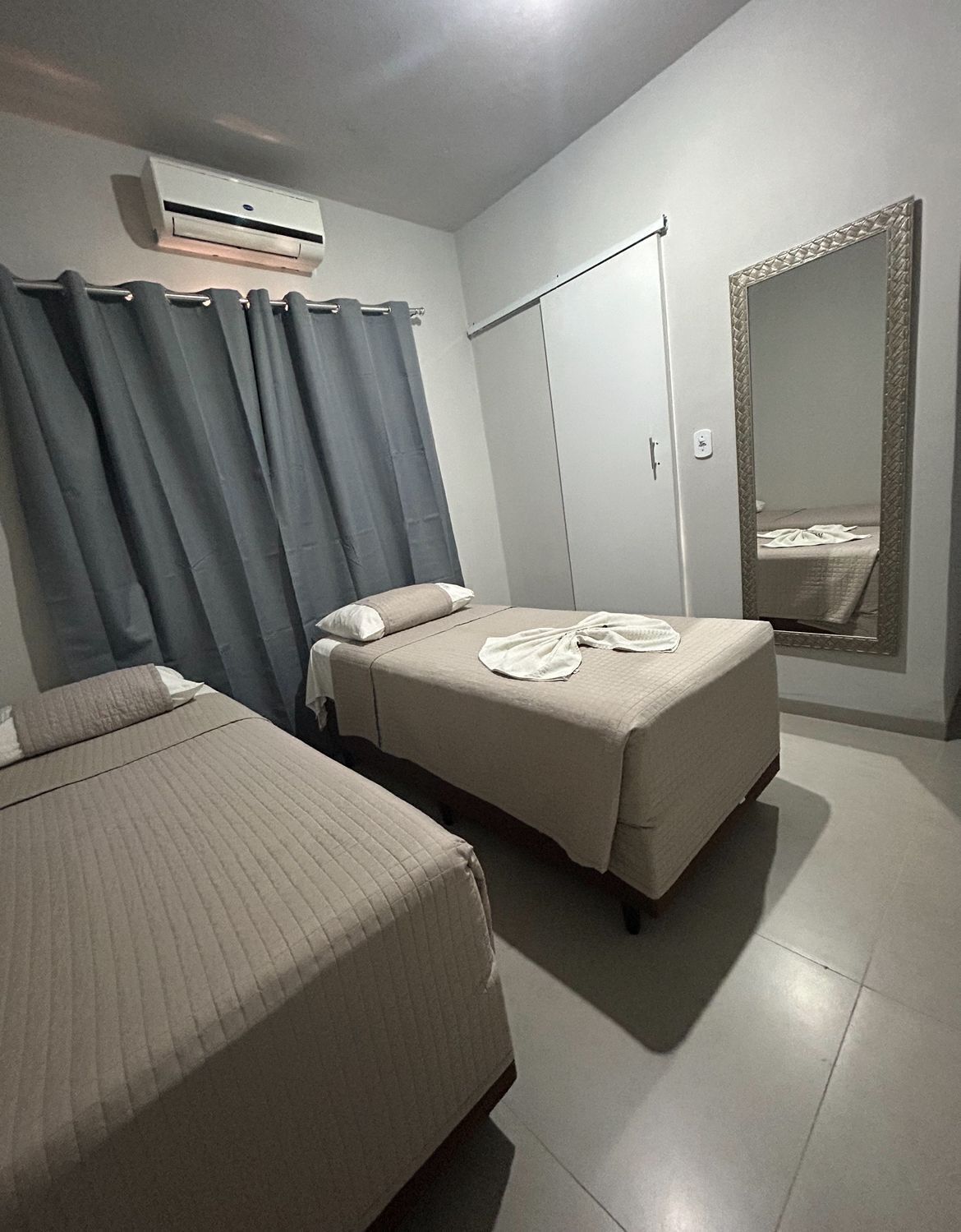 Quarto com duas camas, um guarda-roupa, um ar condicionado e um espelho.