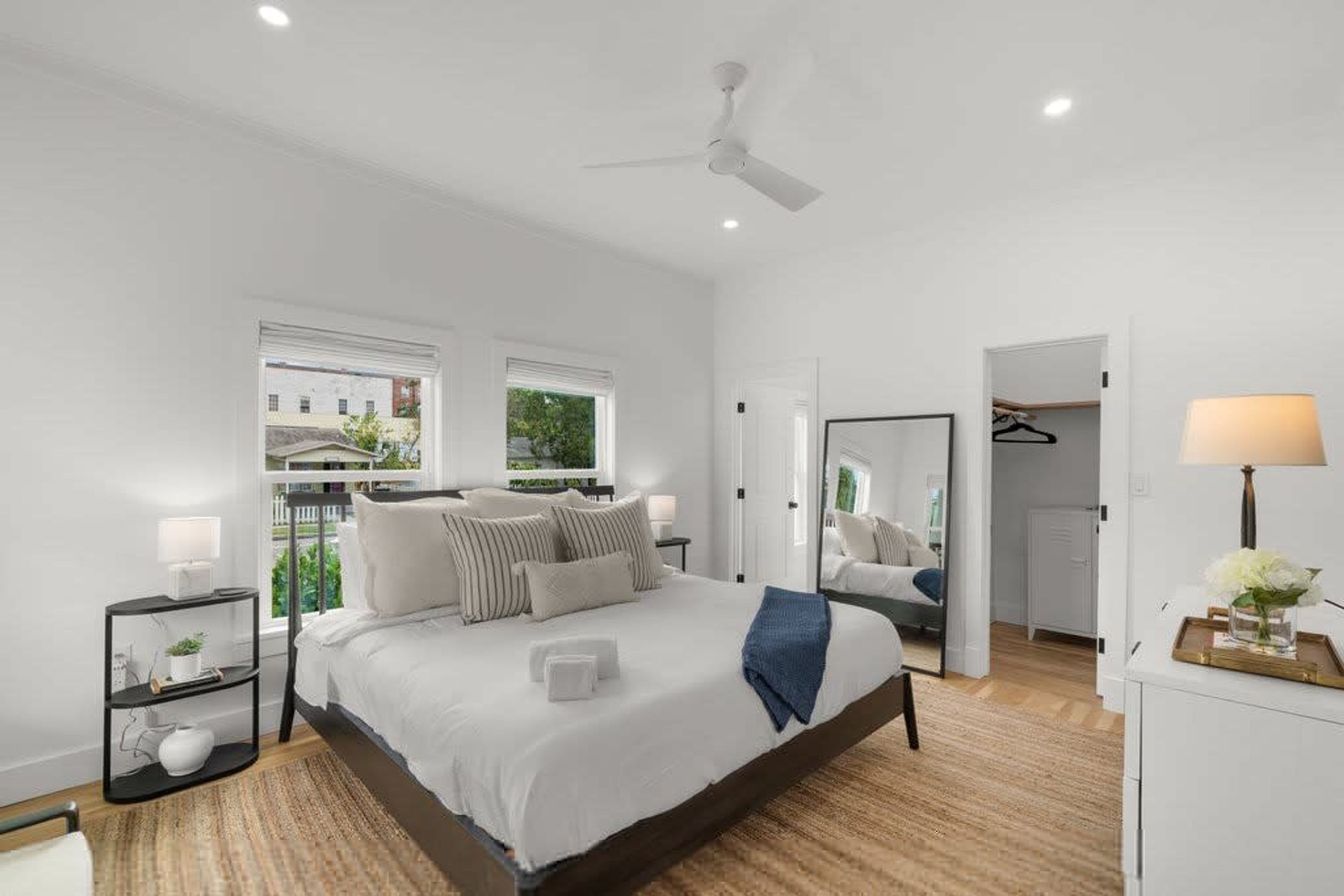 Quarto moderno com uma cama grande, mesas de cabeceira, ventilador de teto e vista para o exterior.
