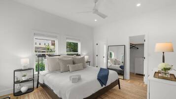 Quarto moderno com uma cama grande, mesas de cabeceira, ventilador de teto e vista para o exterior.