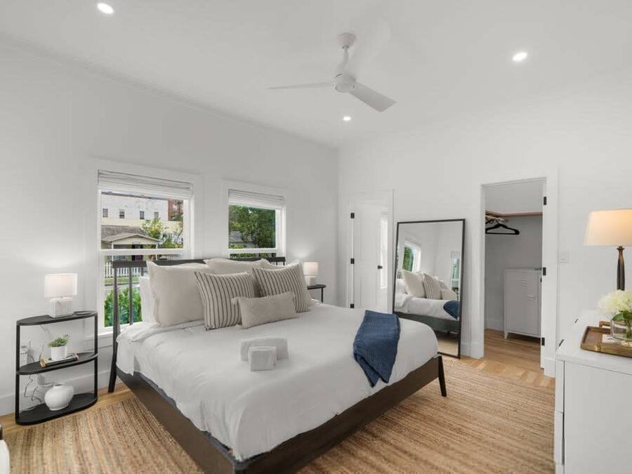 Quarto moderno com uma cama grande, mesas de cabeceira, ventilador de teto e vista para o exterior.