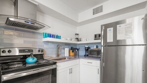 Uma cozinha moderna com eletrodomésticos de aço inoxidável, armários brancos e uma chaleira azul sobre o fogão.