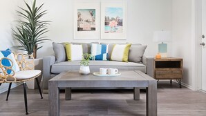 Uma sala de estar com sofá cinzento, mesa de centro, cadeira de vime e planta em vaso.