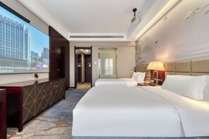 Quarto de hotel com uma cama grande, uma escrivaninha com computador e uma televisão exibindo uma vista urbana.