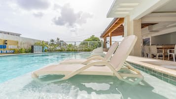 Piscina com espreguiçadeiras, área de estar coberta e placa indicando 'Hotel in the Beach'.