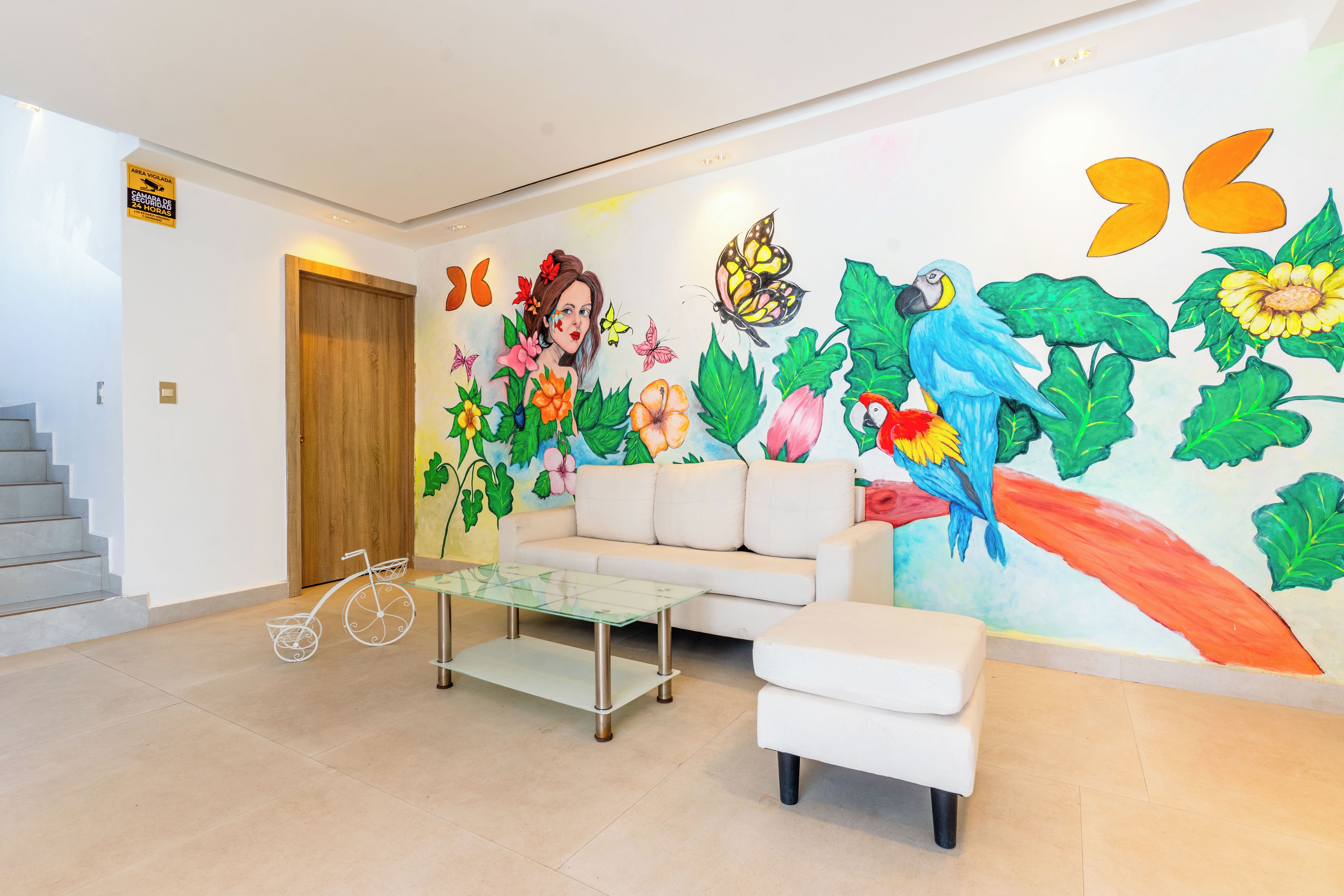 Um lobby moderno com um mural, um sofá, uma mesa de centro de vidro e uma bicicleta.