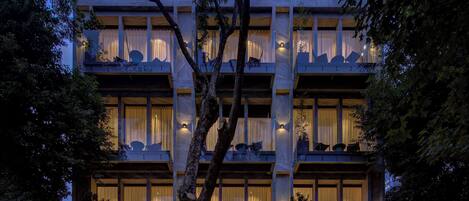 Um hotel com várias andares, varandas, janelas amplas e uma árvore em primeiro plano.