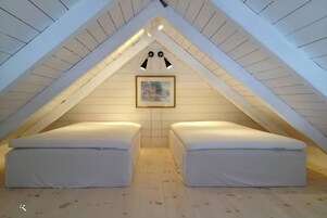 Um quarto de sótão pequeno com duas camas brancas, ripas de madeira no teto e um quadro na parede.