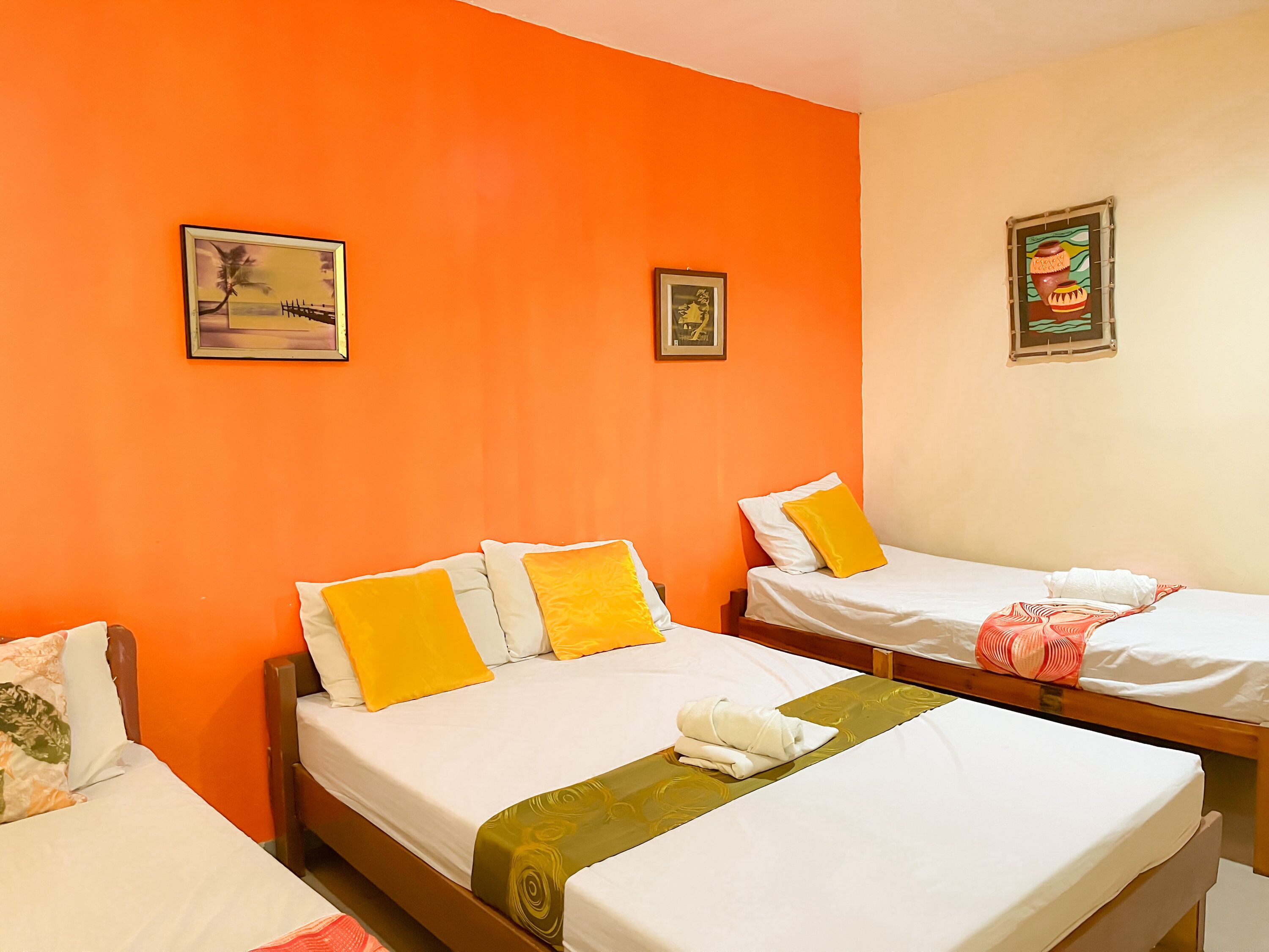 Quarto de hotel com duas camas, paredes laranja e obras de arte.