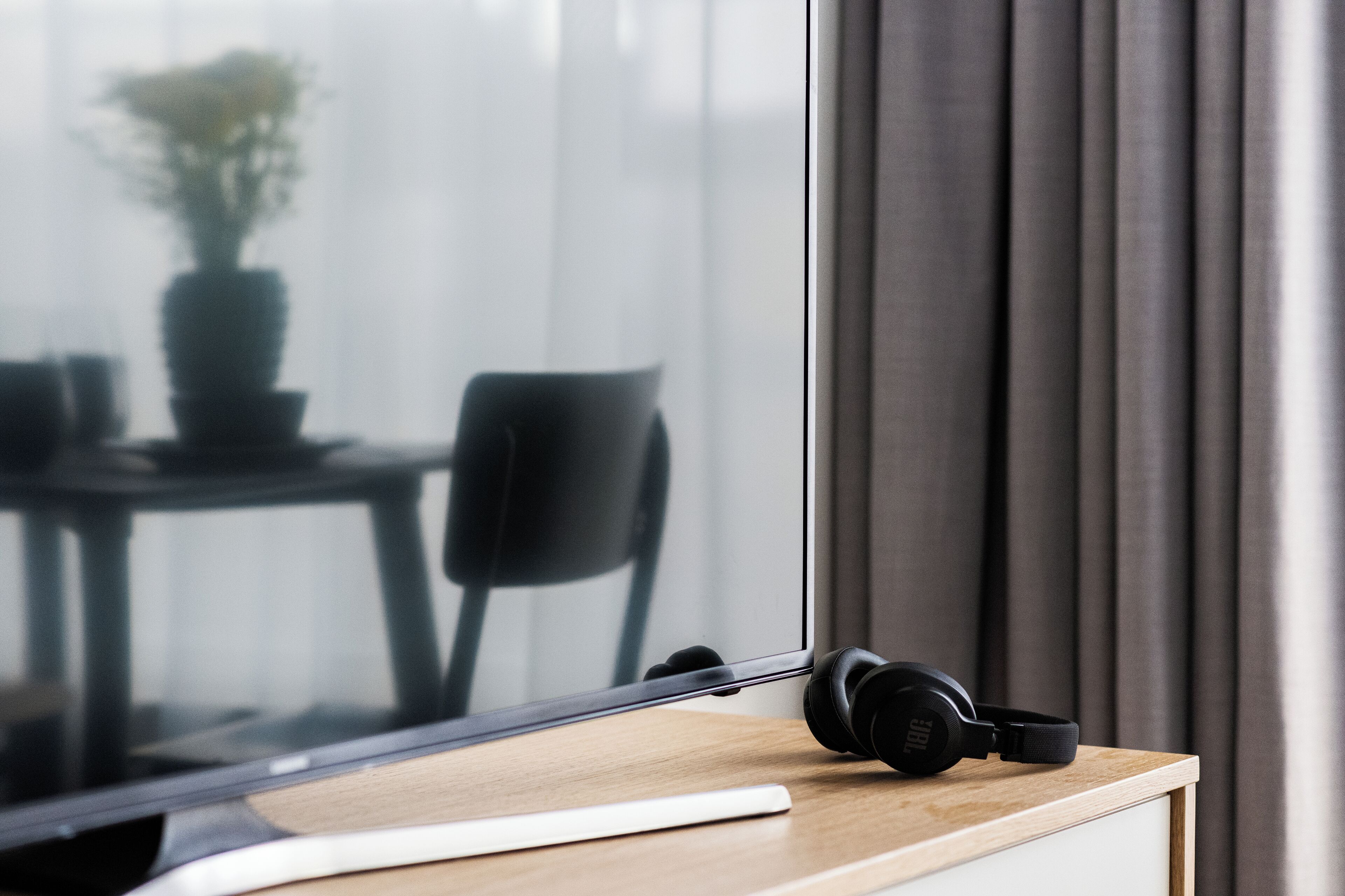 Um par de fones de ouvido sobre uma mesa de madeira com uma janela de vidro e uma planta em vaso ao fundo.