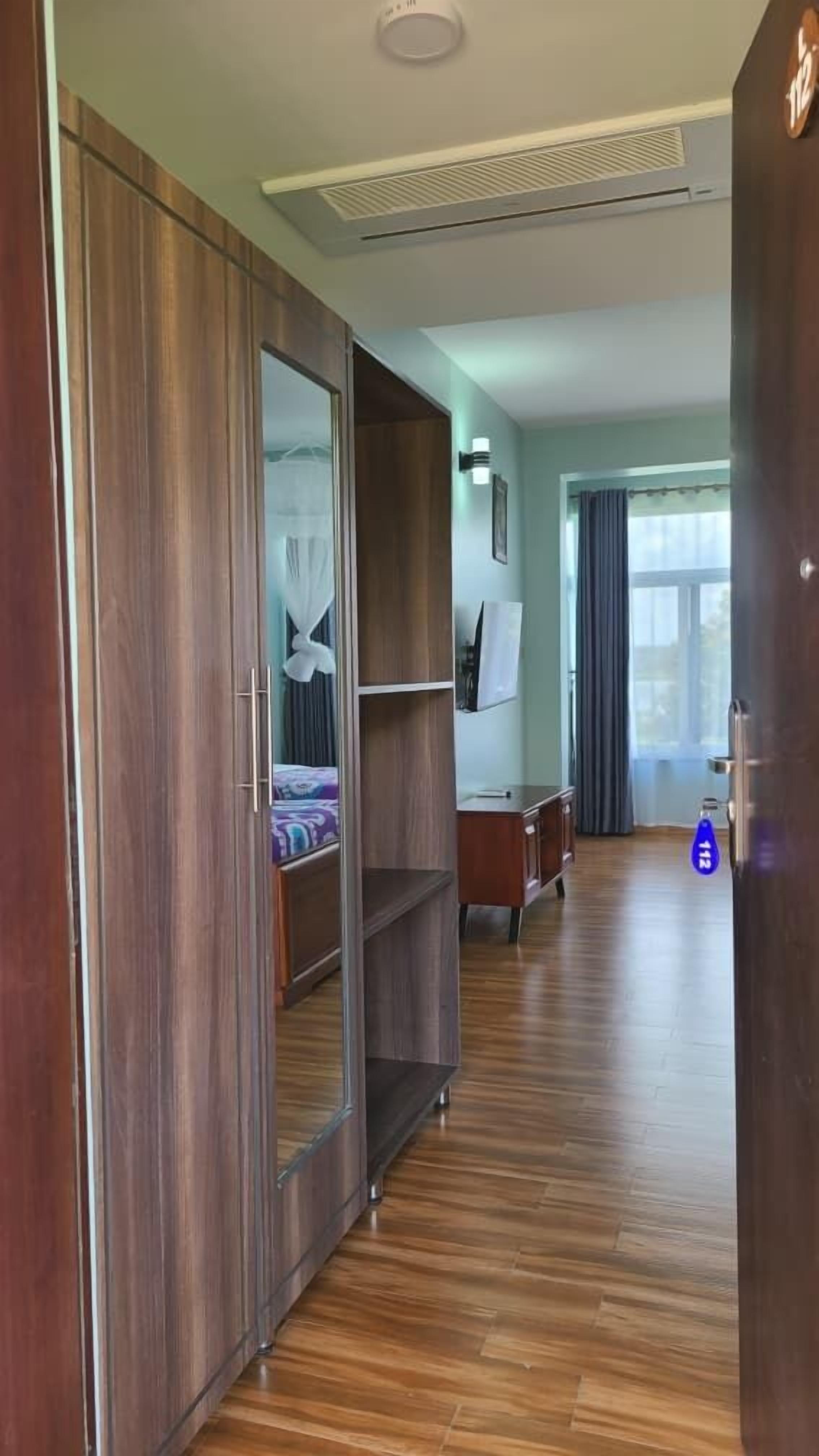 Quarto de hotel com guarda-roupa de madeira, cama com dossel, escrivaninha com cadeira e janela com cortinas.