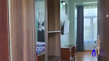 Quarto de hotel com guarda-roupa de madeira, cama com dossel, escrivaninha com cadeira e janela com cortinas.
