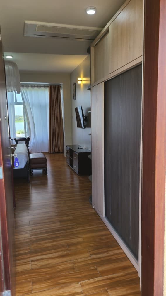 Corredor de hotel com piso de madeira, uma cama, uma escrivaninha e uma televisão na parede.