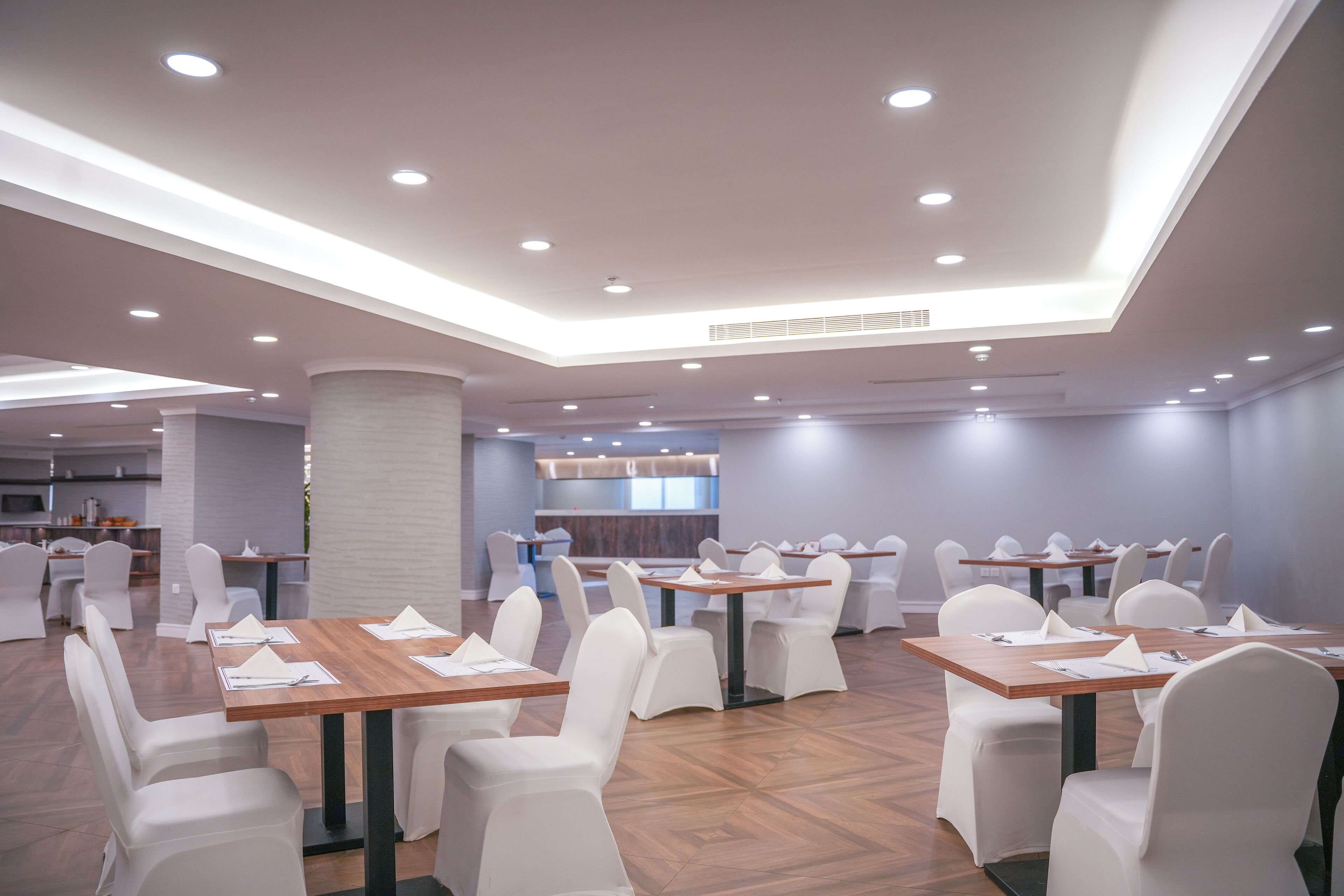 Uma sala de conferências moderna com cadeiras brancas, mesas de madeira e iluminação embutida no teto.
