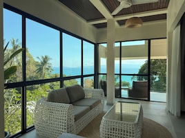 Quarto moderno com amplas janelas, um sofá, mesa de centro de vidro e ventilador de teto.