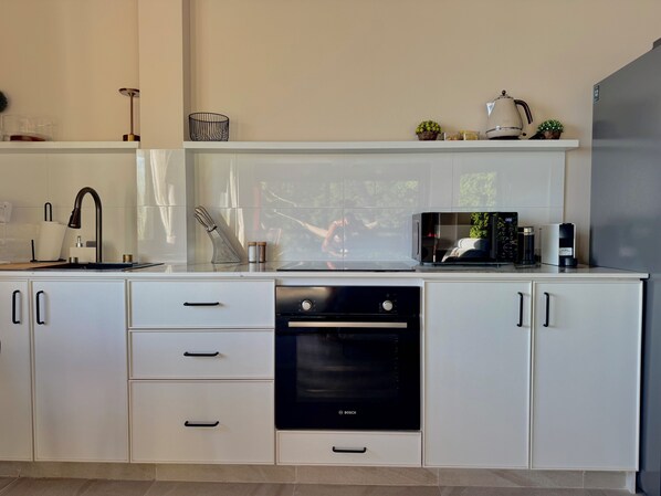 Cozinha moderna com armários brancos, forno Bosch, micro-ondas e cafeteira.