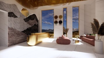 Um interior moderno com uma grande escultura de pedra, um balcão de recepção dourado e uma área de estar com vista para montanhas através de grandes janelas.