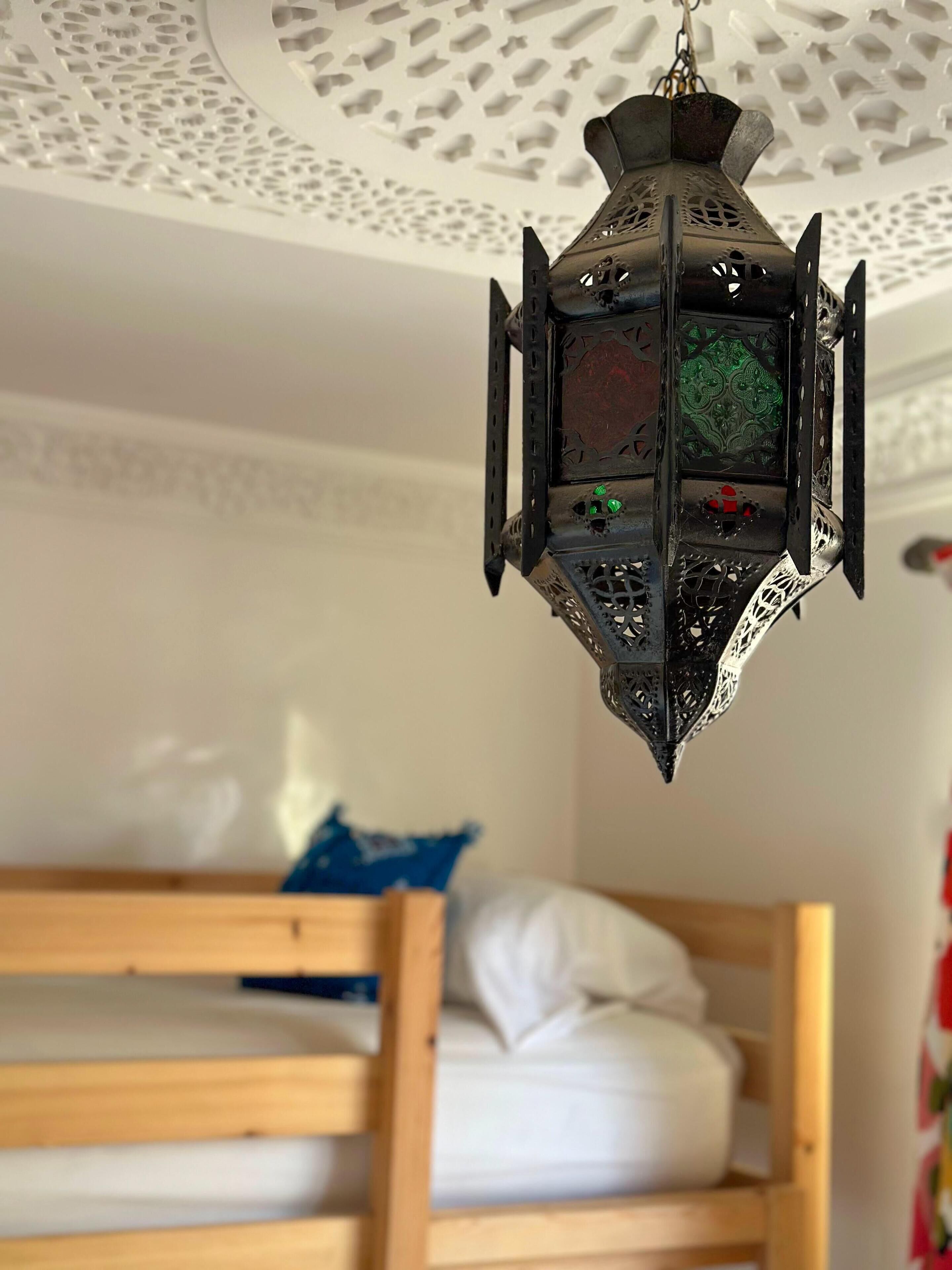 Quarto com uma cama de solteiro e um candeeiro suspenso com detalhes metálicos elaborados.