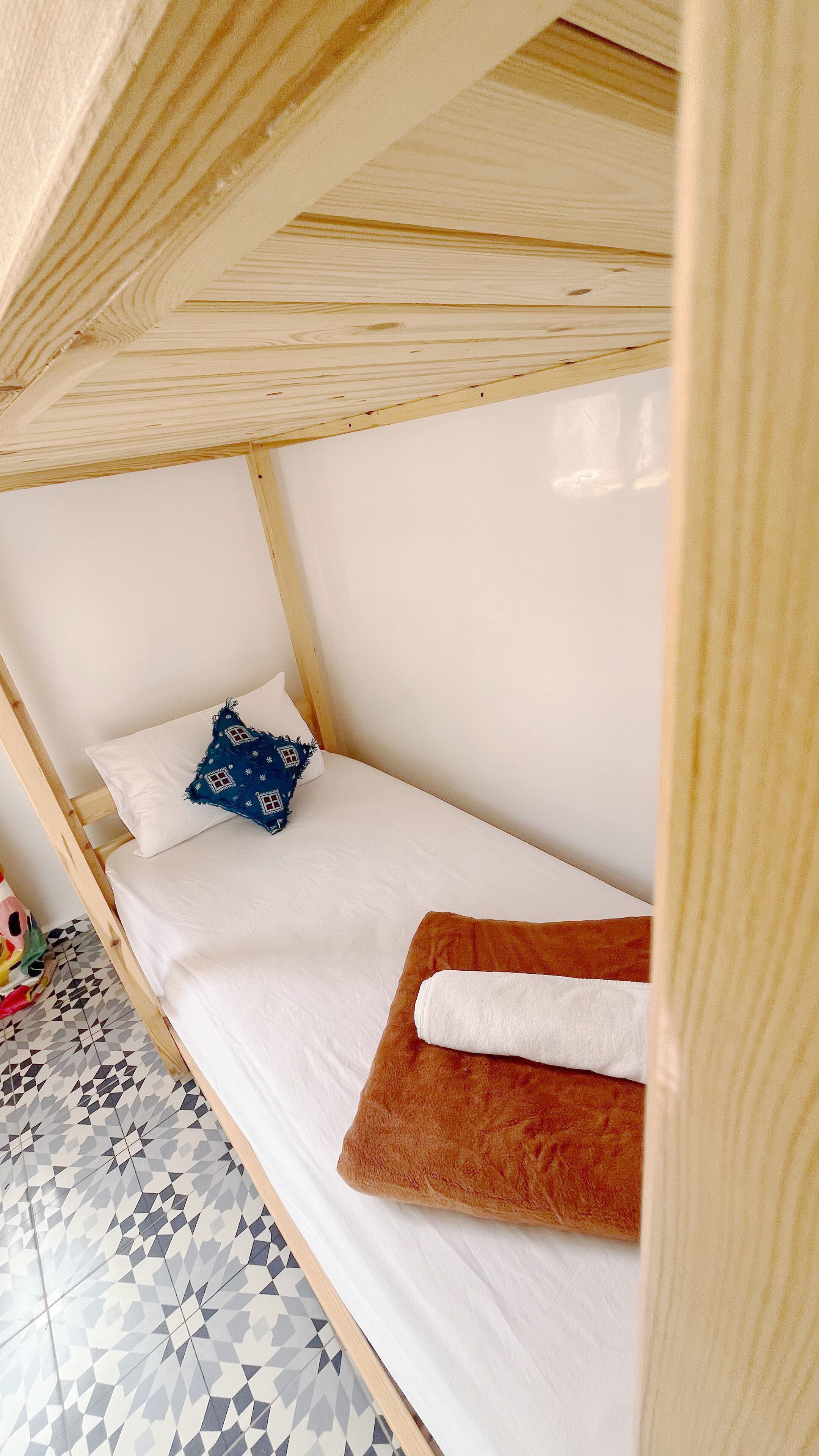 Uma cama de solteiro com colchão branco, travesseiro azul e manta marrom.