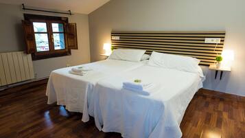 Quarto de hotel com uma cama grande, duas mesas de cabeceira, uma janela com persianas de madeira e um radiador na parede.