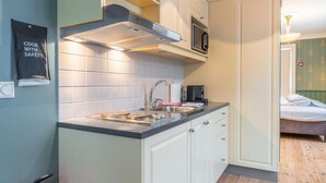 Uma cozinha compacta com armários brancos, uma pia de aço inoxidável e um micro-ondas. Um extintor de incêndio está fixado na parede à esquerda.