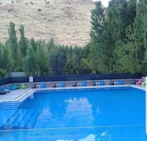Uma piscina com água azul, rodeada por um muro de pedra e diversos assentos de bean bag coloridos.