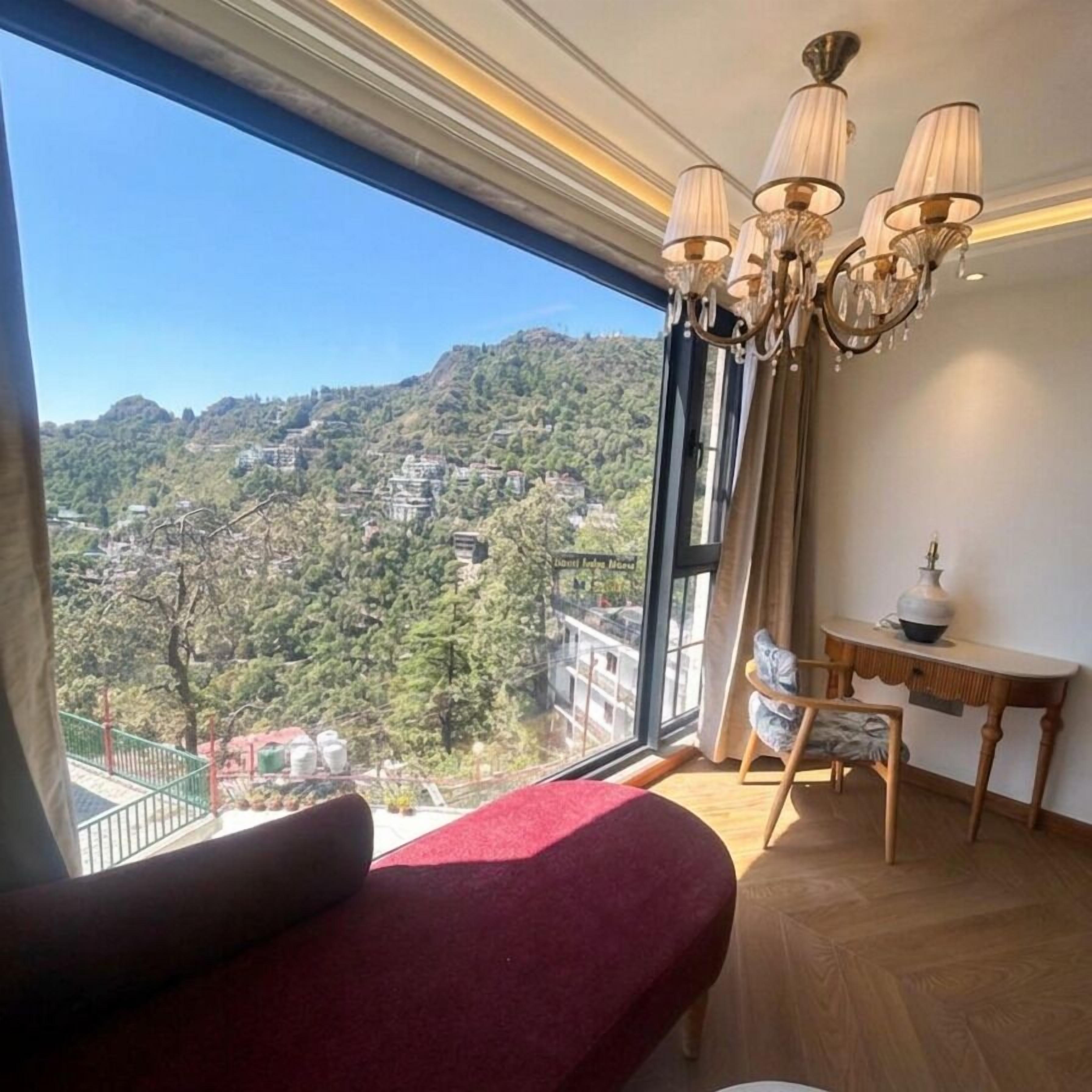 Quarto com uma janela grande, sofá vermelho, mesa de madeira e um candelabro.