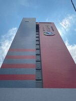 Um edifício alto com fachada vermelha e cinza, exibindo um logotipo e texto na lateral.