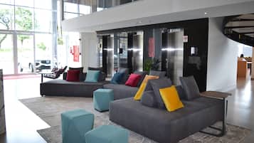 Um hall moderno com dois sofás cinzentos, pufes verde-água e uma variedade de almofadas coloridas.