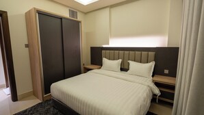 Quarto de hotel com uma cama grande, guarda-roupa, mesa de cabeceira e apoio para luminária.