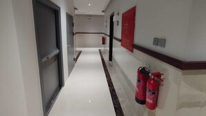 Corredor com extintor fixado na parede, alarme de incêndio e uma porta à esquerda.