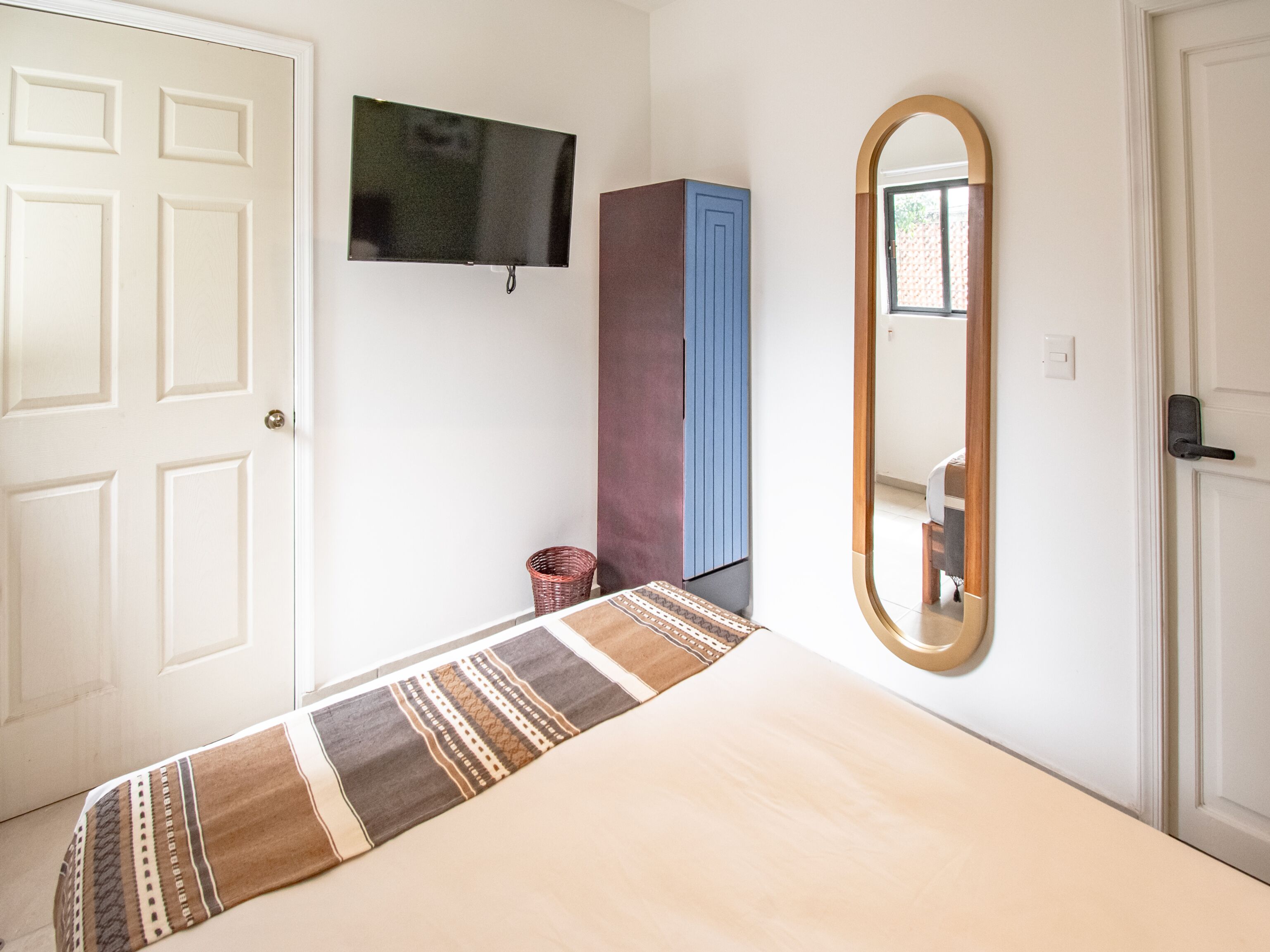 Quarto com cama, televisão na parede, guarda-roupa, espelho e porta.