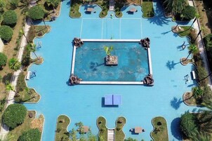 Vista aérea de uma piscina com uma ilha central, rodeada por palmeiras e espreguiçadeiras.
