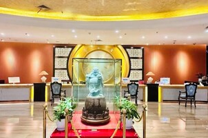 Uma área de recepção com uma estátua, balcão de atendimento, cadeiras e tapete vermelho.