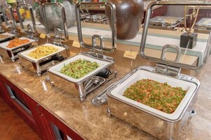 Buffet com diversos pratos em bandejas de metal, cada uma com etiqueta.