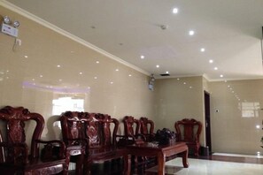 Uma sala de jantar com uma mesa comprida e cadeiras, teto com iluminação embutida e uma porta ao fundo.