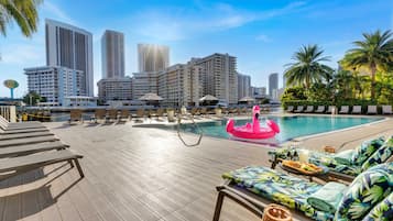 Uma piscina no terraço com espreguiçadeiras, um flutuador em formato de flamingo rosa e um horizonte urbano ao fundo.
