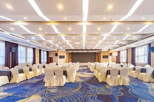 Uma sala de conferências com fileiras de cadeiras, um palco e piso coberto de carpete.