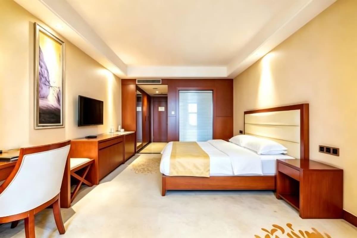 Quarto de hotel com cama, escrivaninha, cadeira, televisão e porta que dá para outro cômodo.
