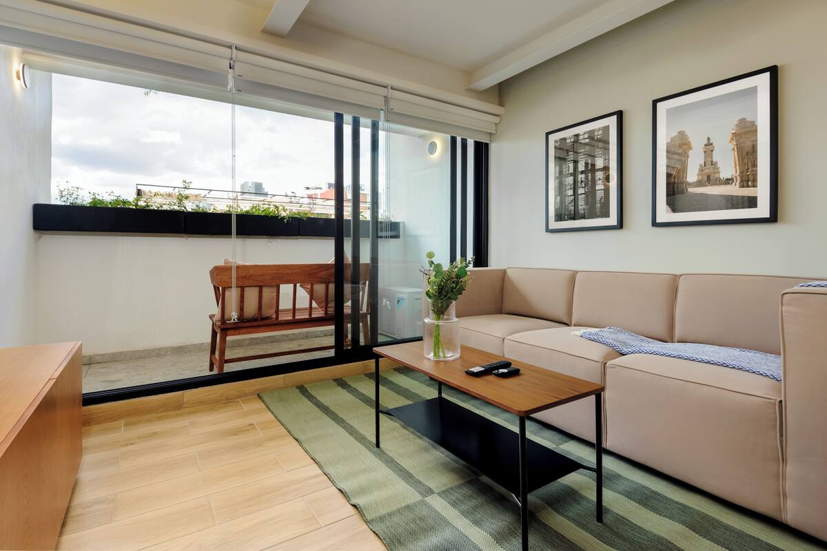 Uma sala de estar moderna com um sofá, uma mesa de madeira, um controle remoto e um vaso com flores.