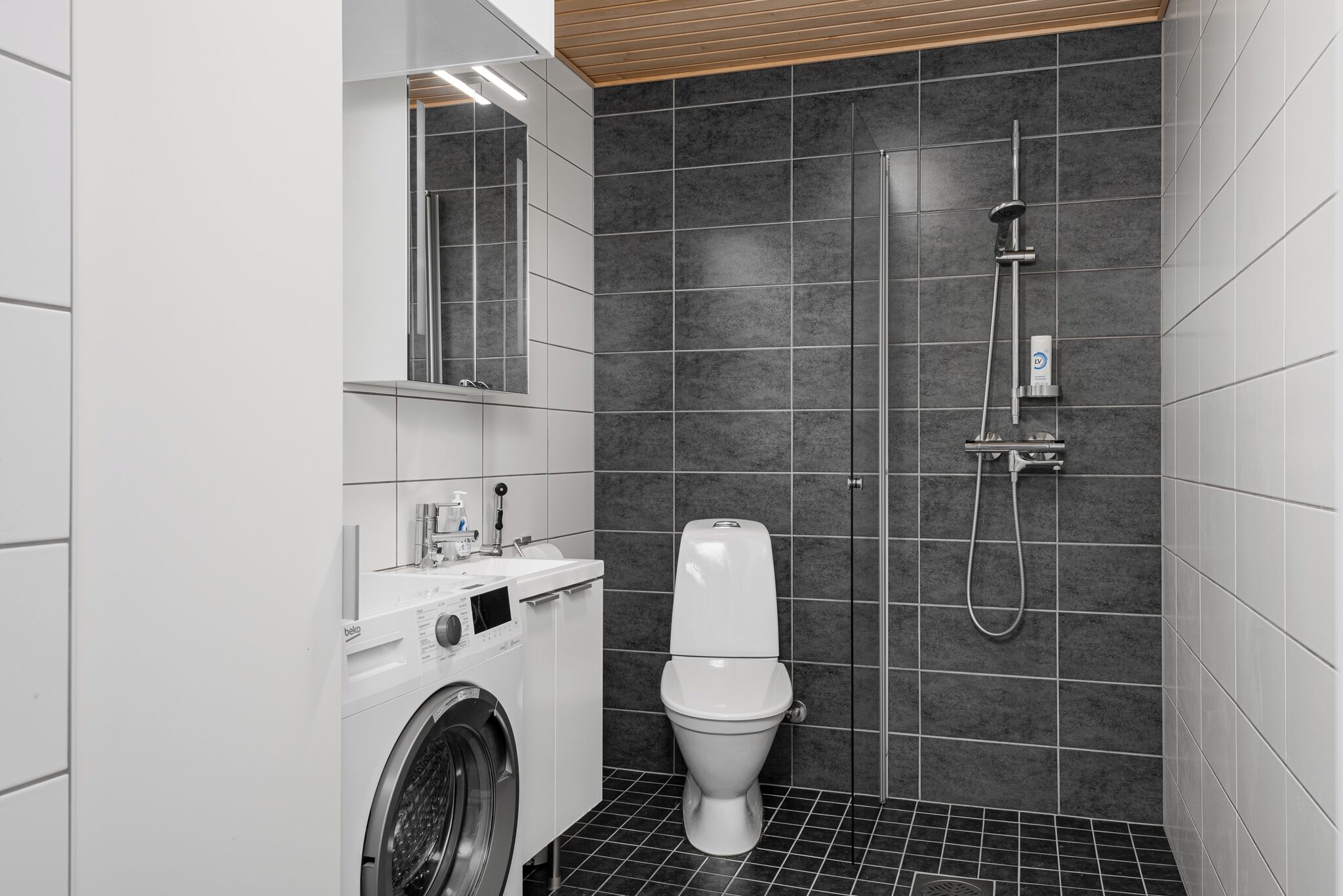 Uma casa de banho moderna com máquina de lavar roupa, sanita e chuveiro.