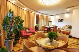 Quarto de hotel com parede curva, área de refeições e diversas opções de assento, incluindo um sofá vermelho e cadeiras de vime.