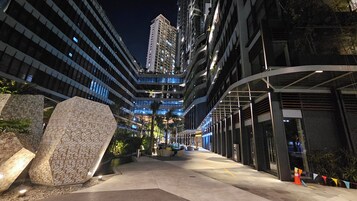 Uma rua urbana moderna à noite, com edifícios altos, um calçadão central e detalhes arquitetônicos iluminados.