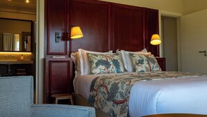 Quarto de hotel com uma cama grande, duas luminárias de cabeceira, um painel de madeira na cabeceira e uma mesa pequena.
